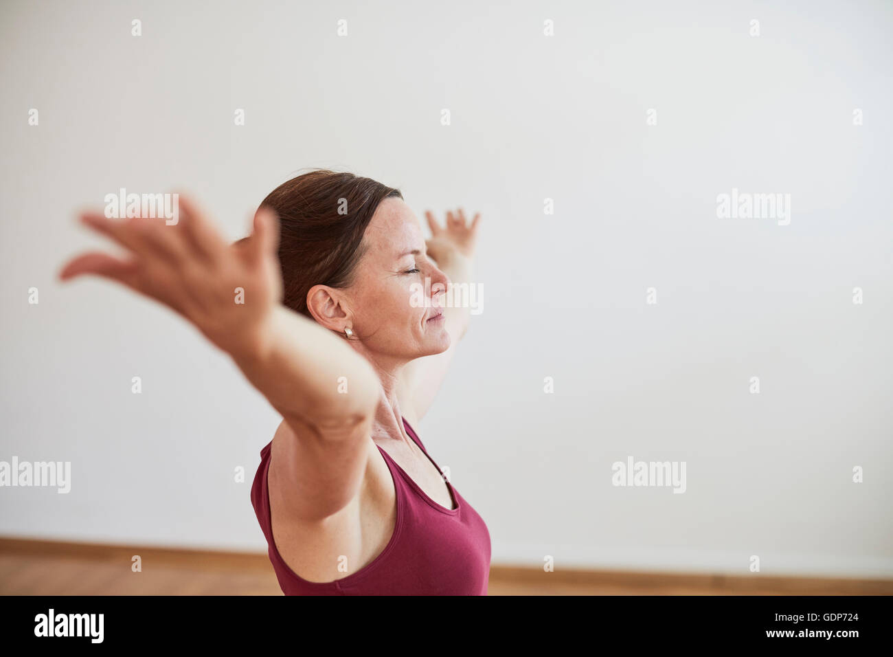 Side view of woman in exercise studio arm raised, eyes closed in yoga ...