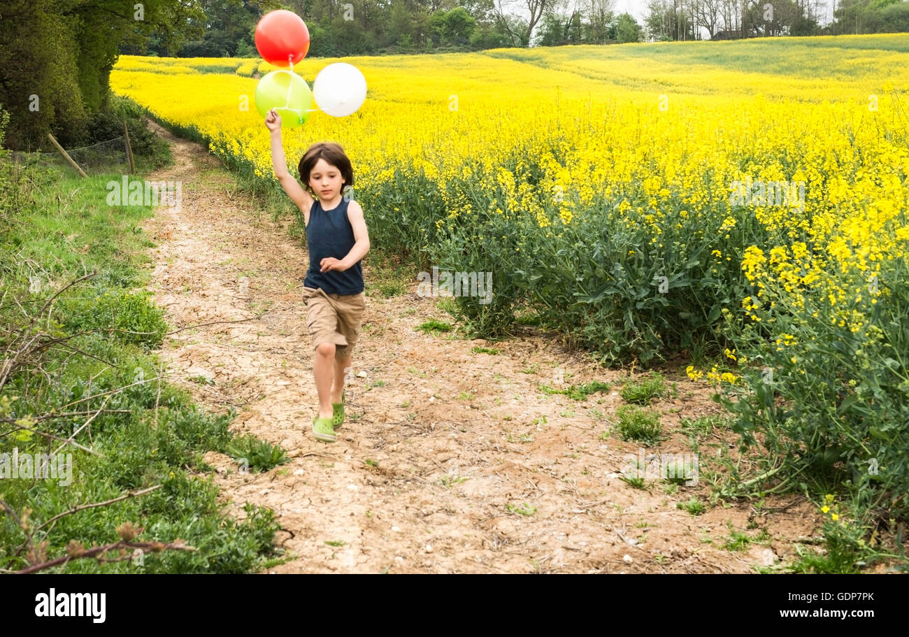 Boy running on yellow flower field track pulling balloons Stock Photo ...