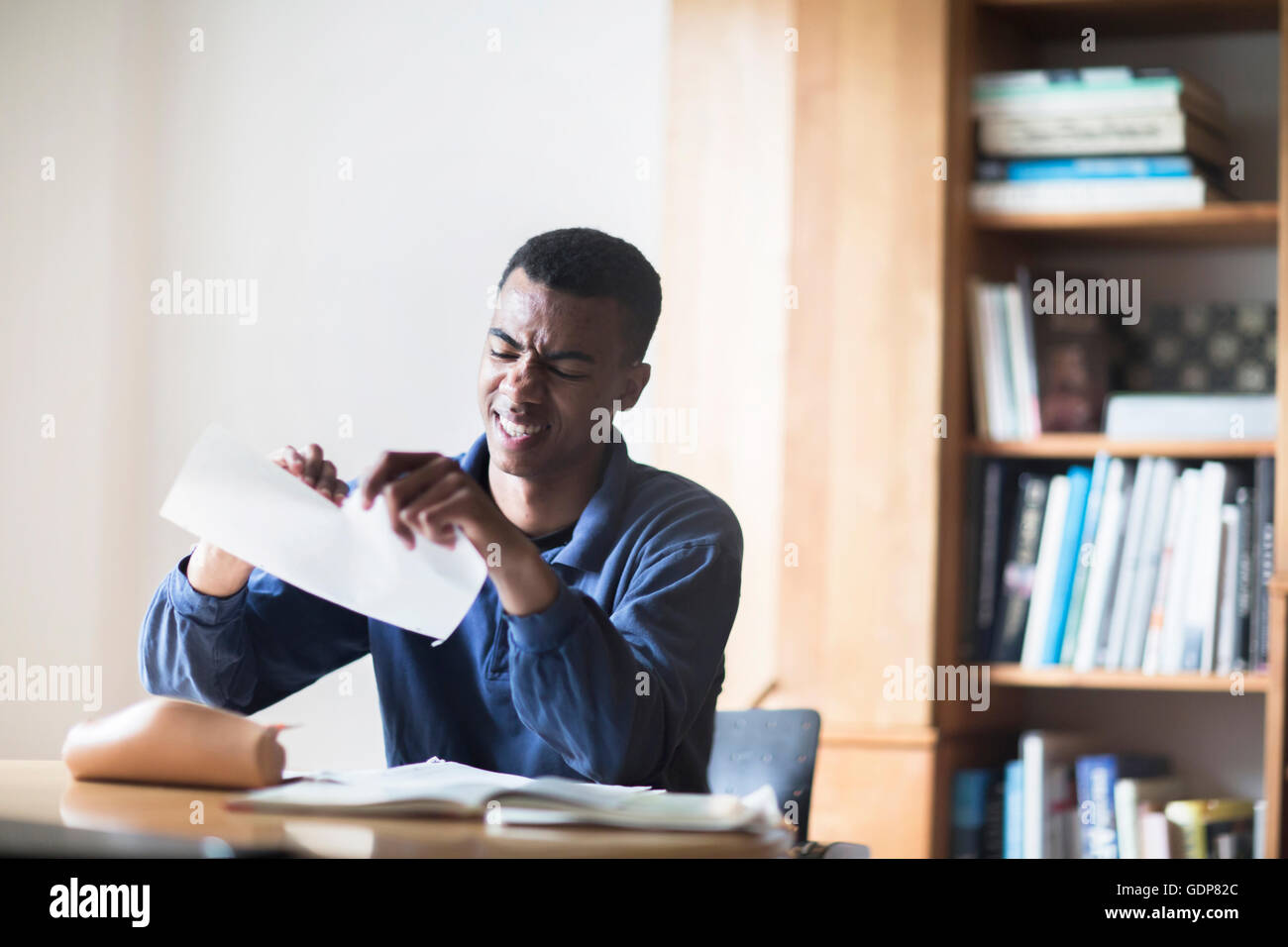 Young male high school student sitting at desk tearing up schoolwork ...
