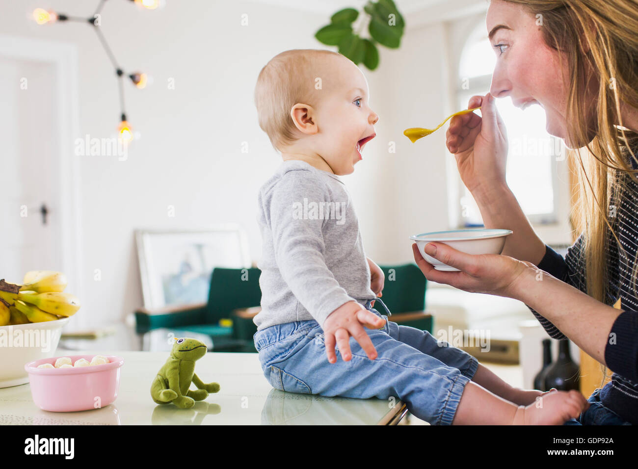 Baby girl mimicking mother whilst eating at kitchen table Stock Photo ...