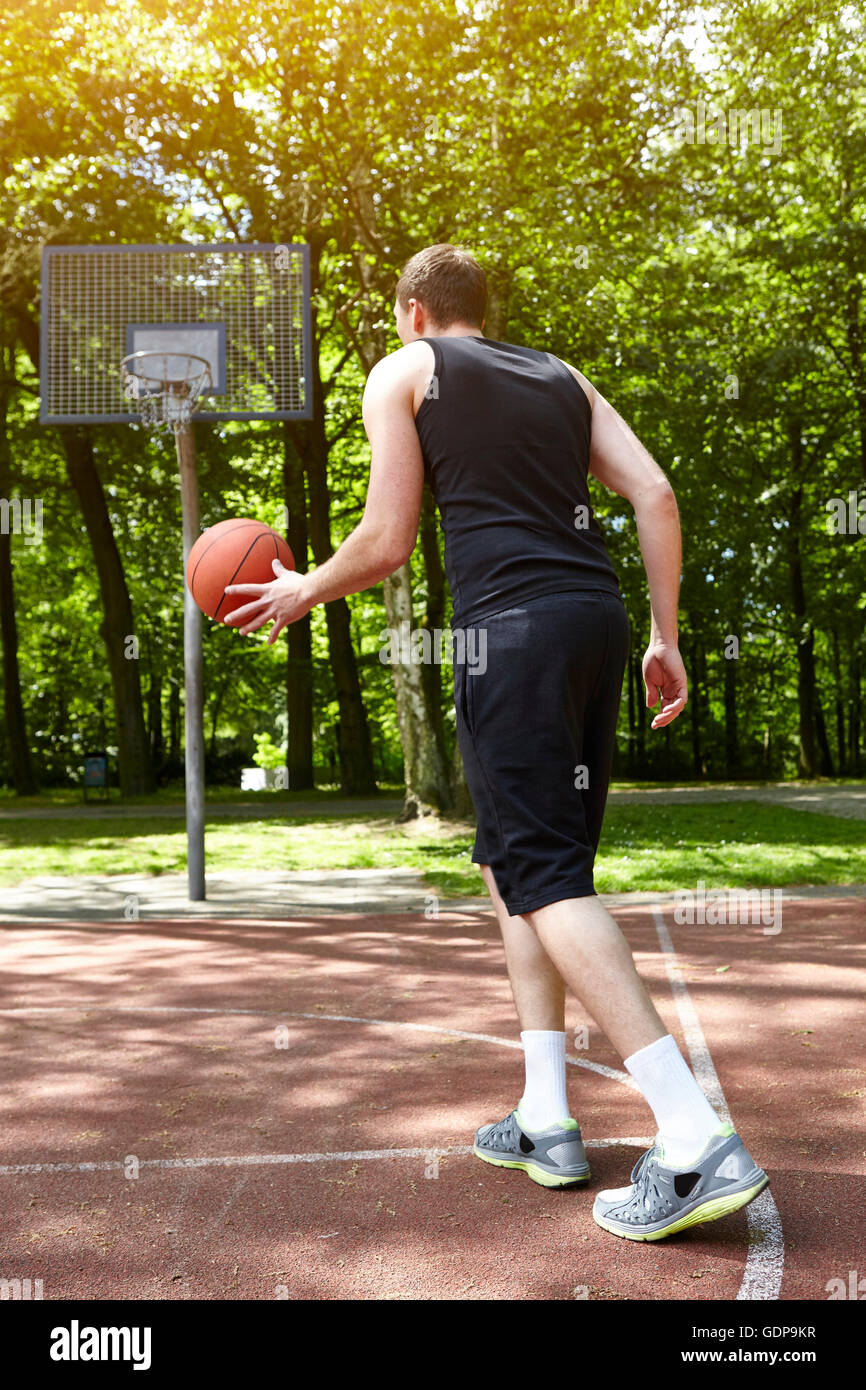 Rear view of young male basketball player running with ball on court ...