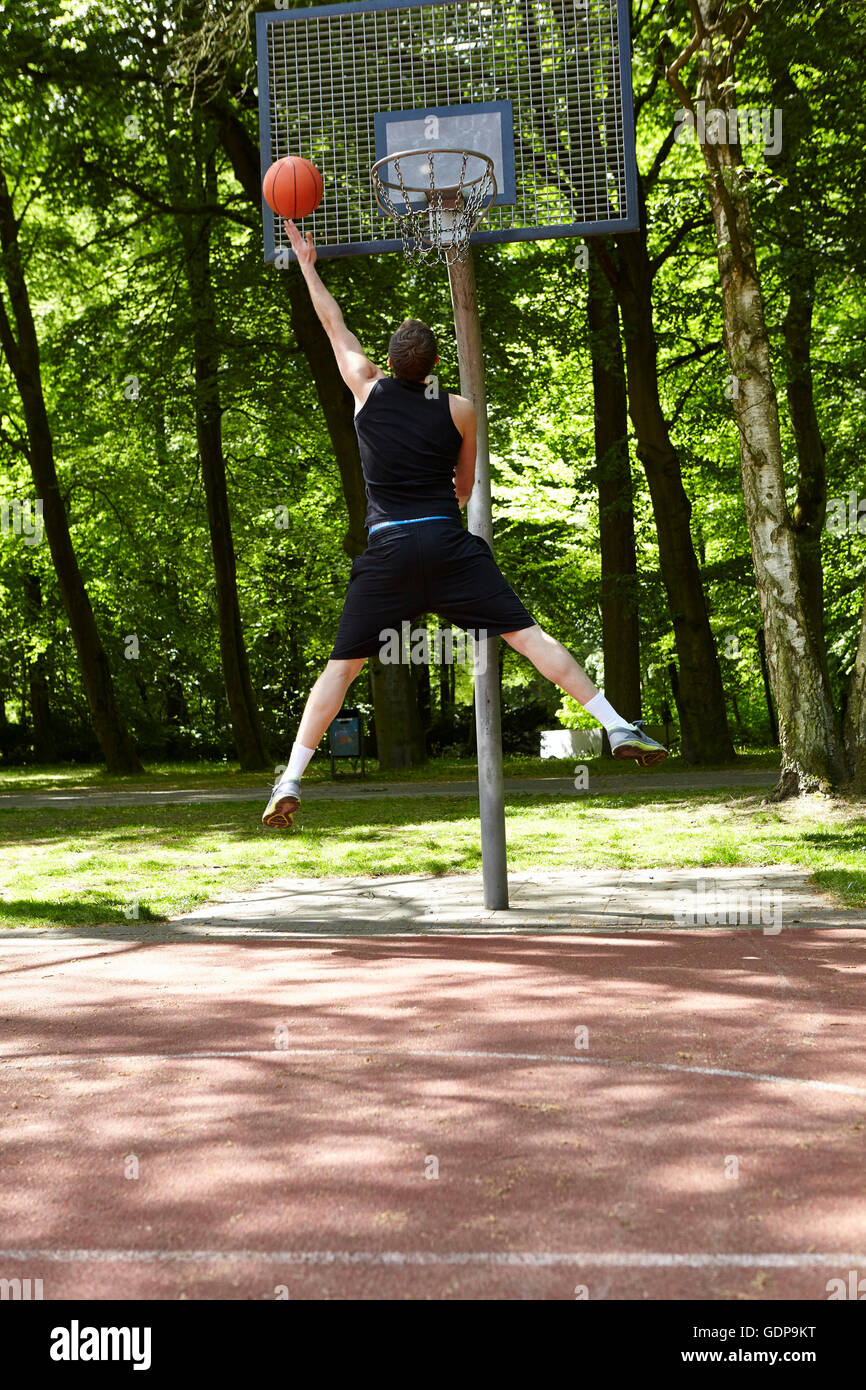 Rear view of young male basketball player jumping and throwing ball at ...