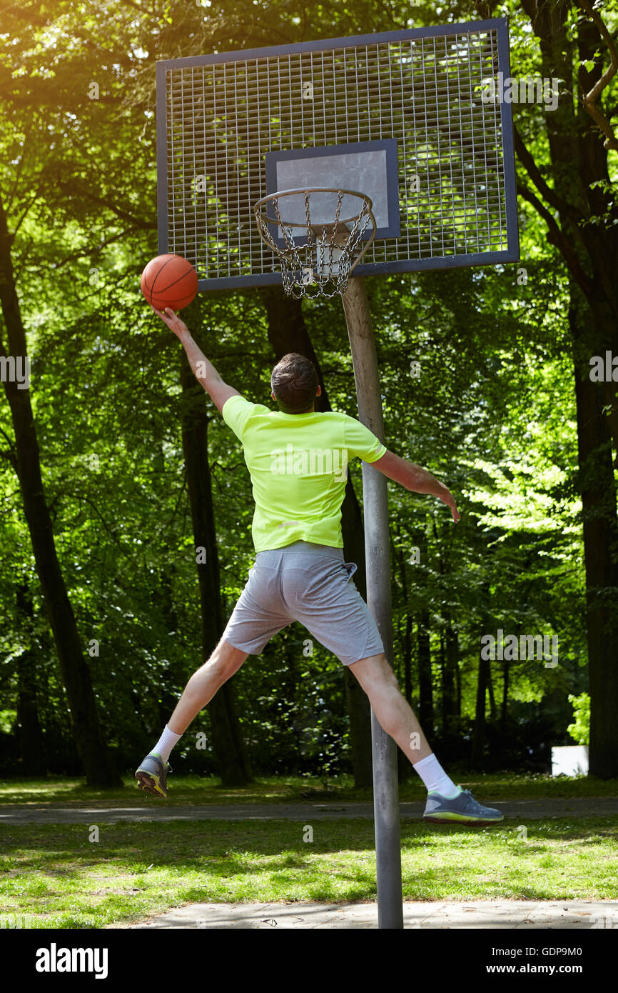 Rear view of young male basketball player jumping and throwing ball at ...