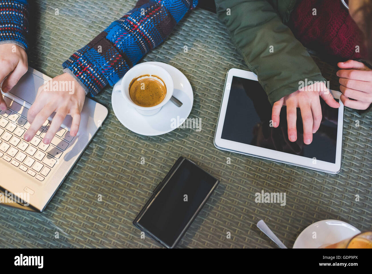 Two women in cafe using laptop,and digital tablet, coffee beside them ...