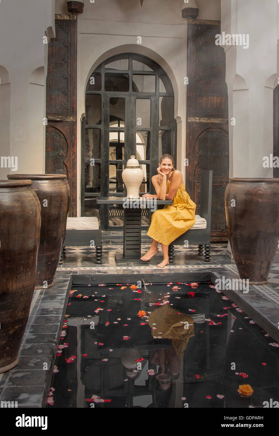 Young woman sitting by petal covered water feature, Marrakesh, Morocco ...