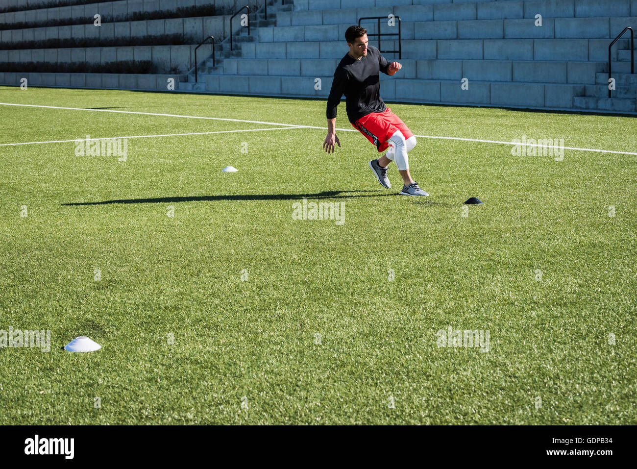 Young man running doing agility training with markers on playing field ...