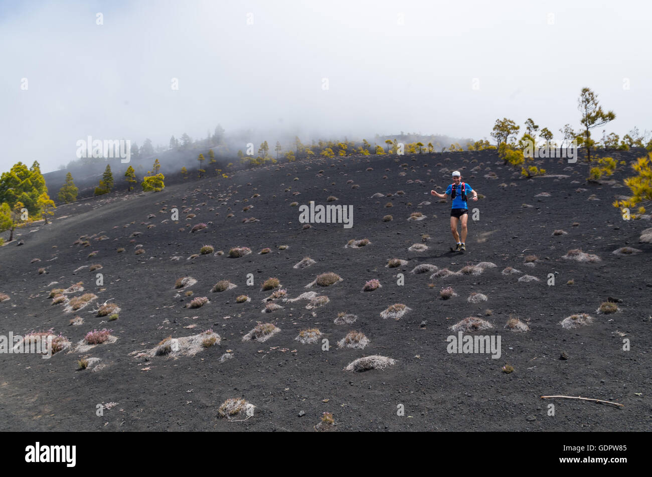Young man running in volcanic landscape with foggy background, La Palma ...