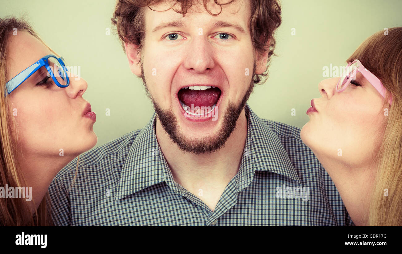 Two pretty women kissing handsome man. Love triangle Stock Photo - Alamy