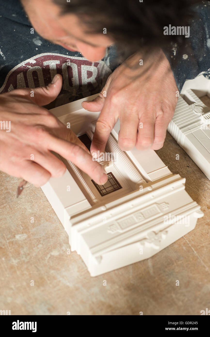 A man sticking a tiny window in place on a plaster scale model ...