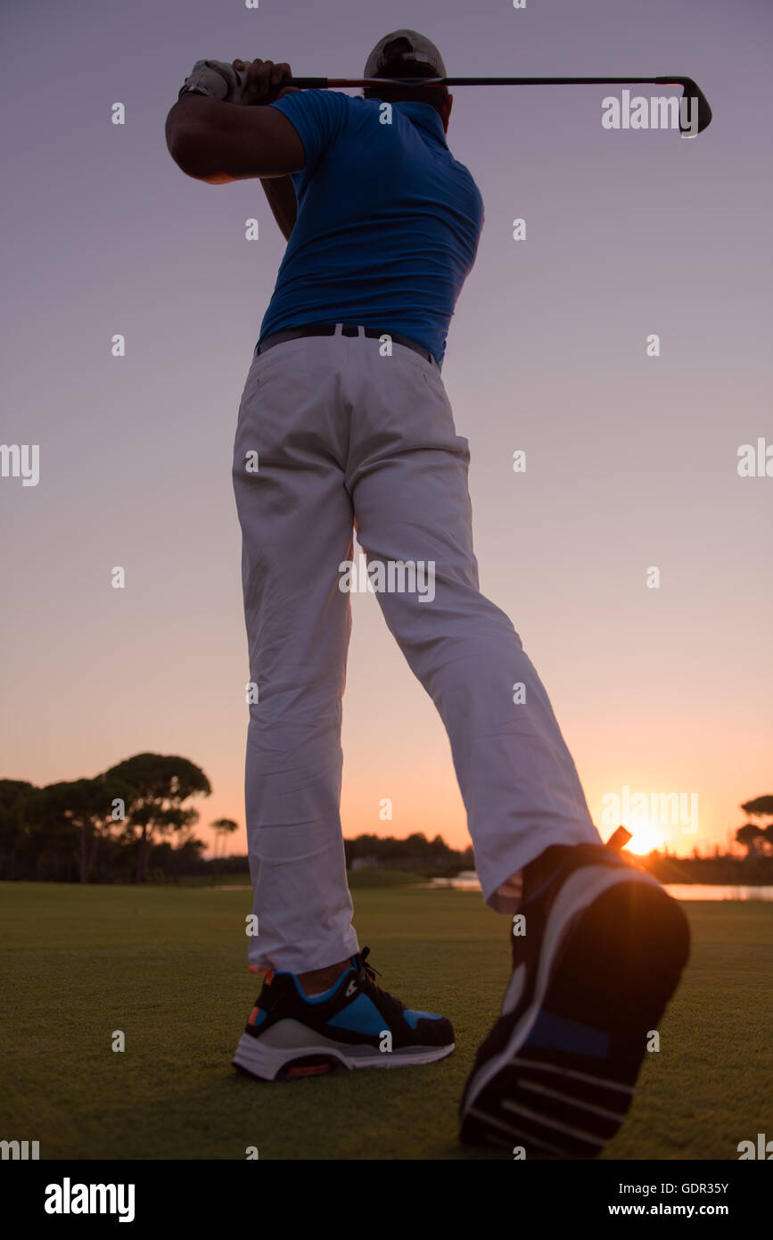 golfer hitting long shot with driver on course at beautiful sunset ...