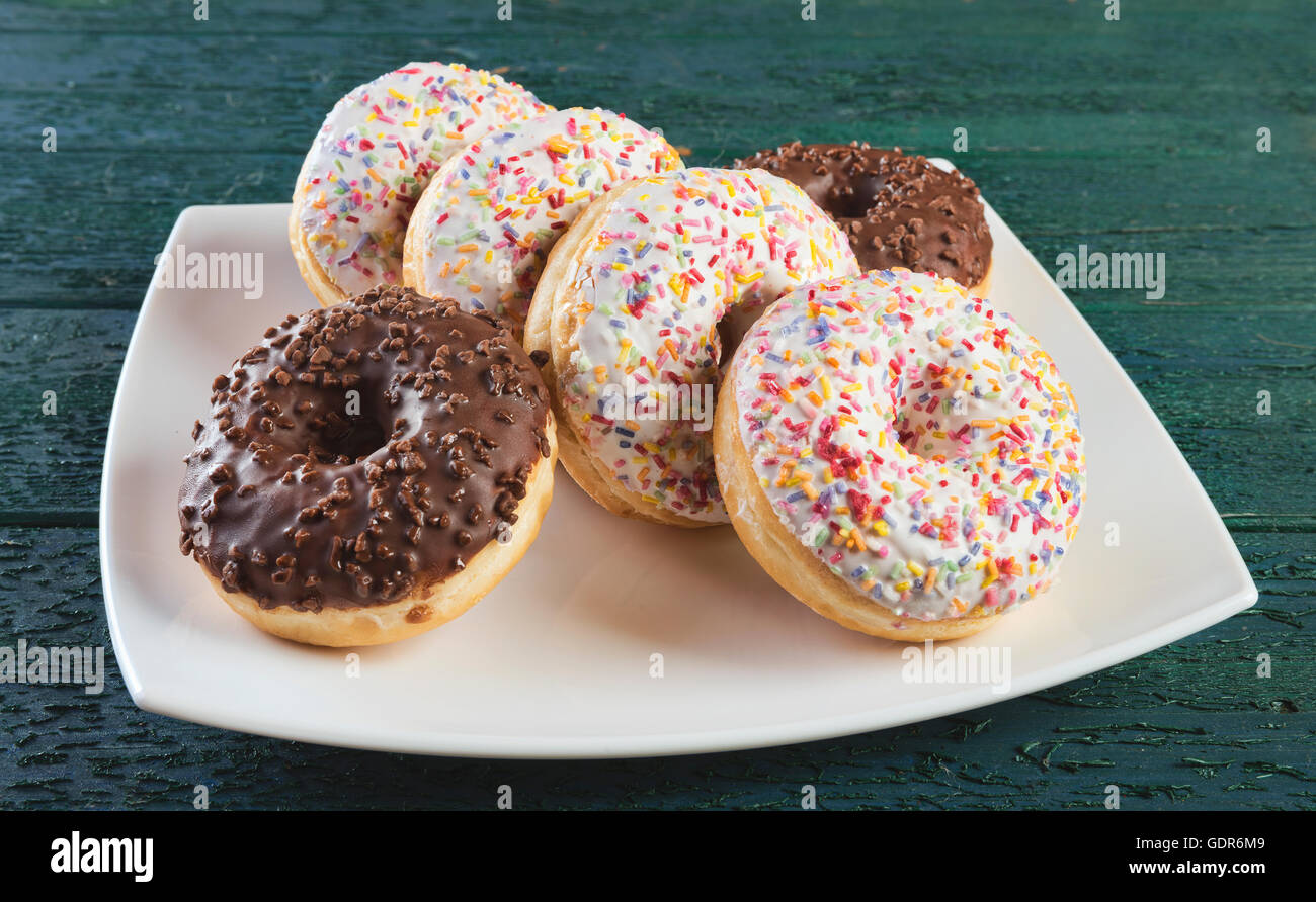 Delicious iced ring donuts on a white plate, sitting on a rustic green ...