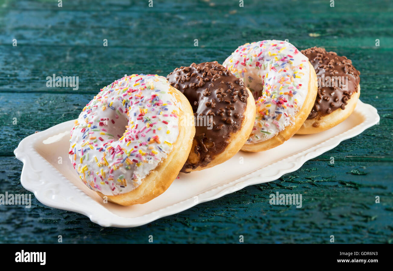 Delicious iced ring donuts on a white plate, sitting on a rustic green ...