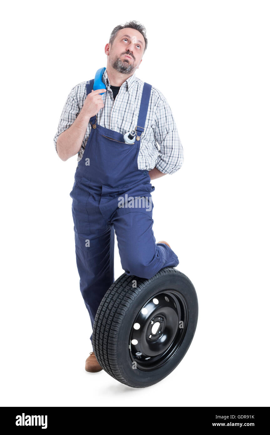 Full body of bored mechanic standing near wheel and holding blue ...