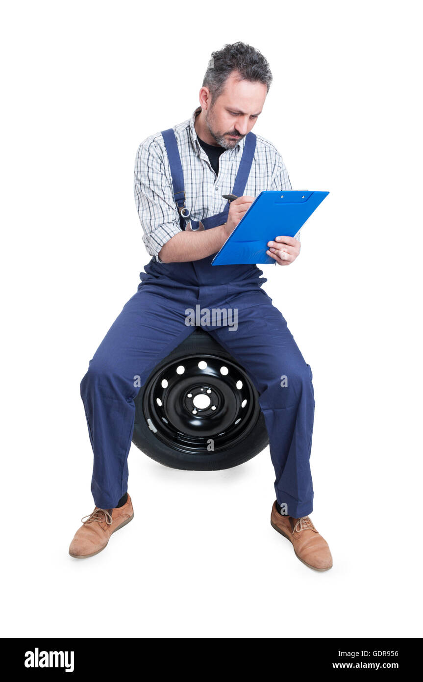 Successful mechanic sitting on wheel and writing on checklist about ...