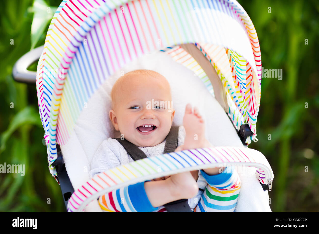 Baby boy in white sweater sitting in white stroller on a walk in park ...