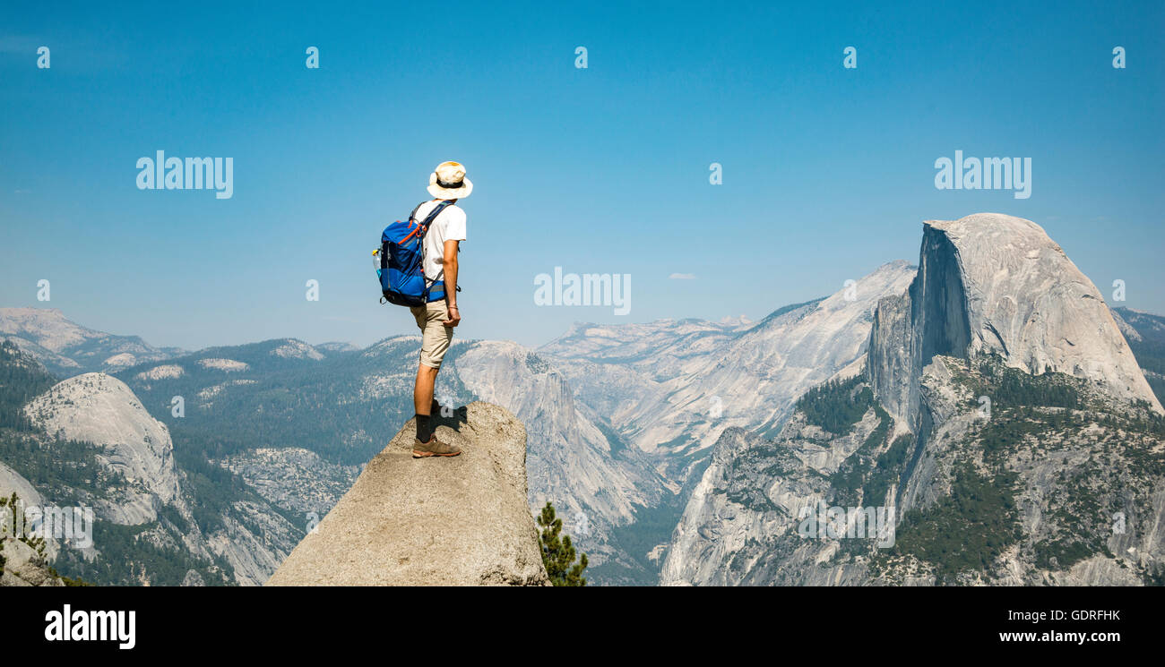 Young man standing on ledge, looking at the Half Dome, view from ...