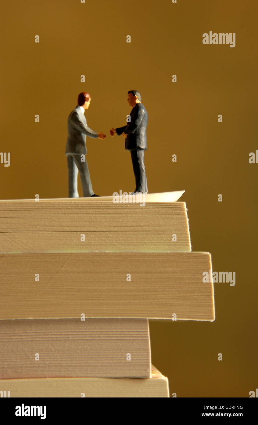 Figurines shaking hands on pile of books Stock Photo - Alamy
