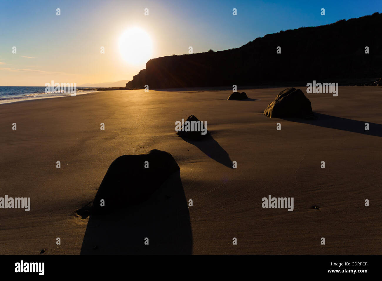 Rocks on a sandy beach sunset Stock Photo - Alamy