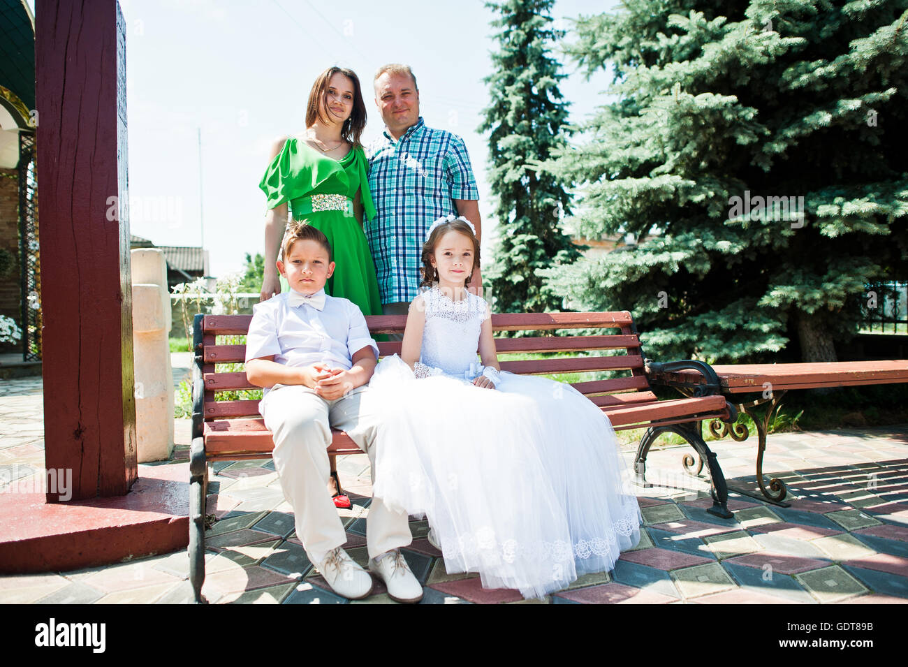 Happy family at first holy communion sitting on bench background church ...