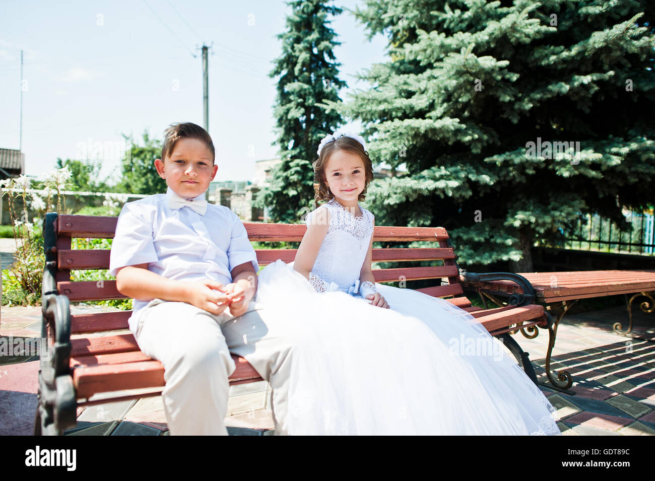 Brother and sister at first holy communion sitting on bench background ...