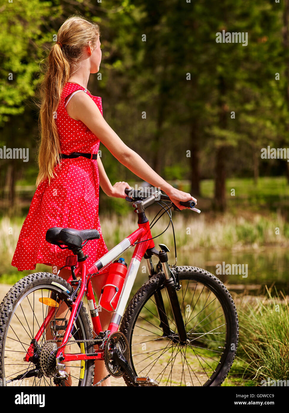 Girl wearing red dress rides bicycle in park Stock Photo - Alamy