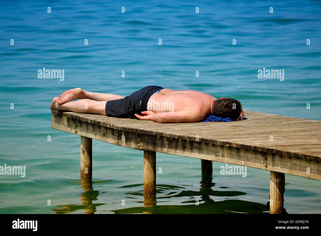 Man resting on a dock by a lake Stock Photo - Alamy