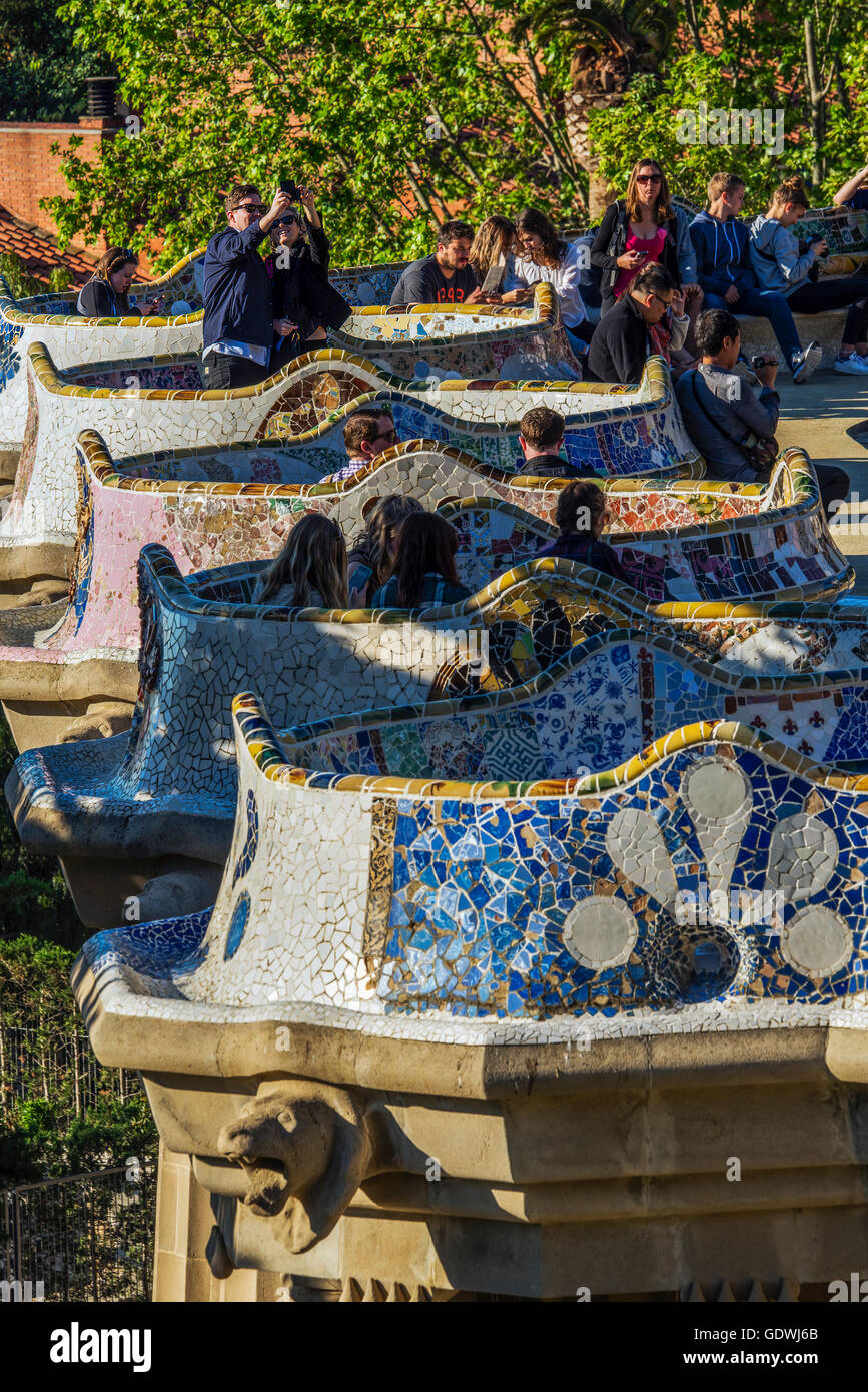 Tourists enjoying the multicolored serpentine bench at Park Guell ...