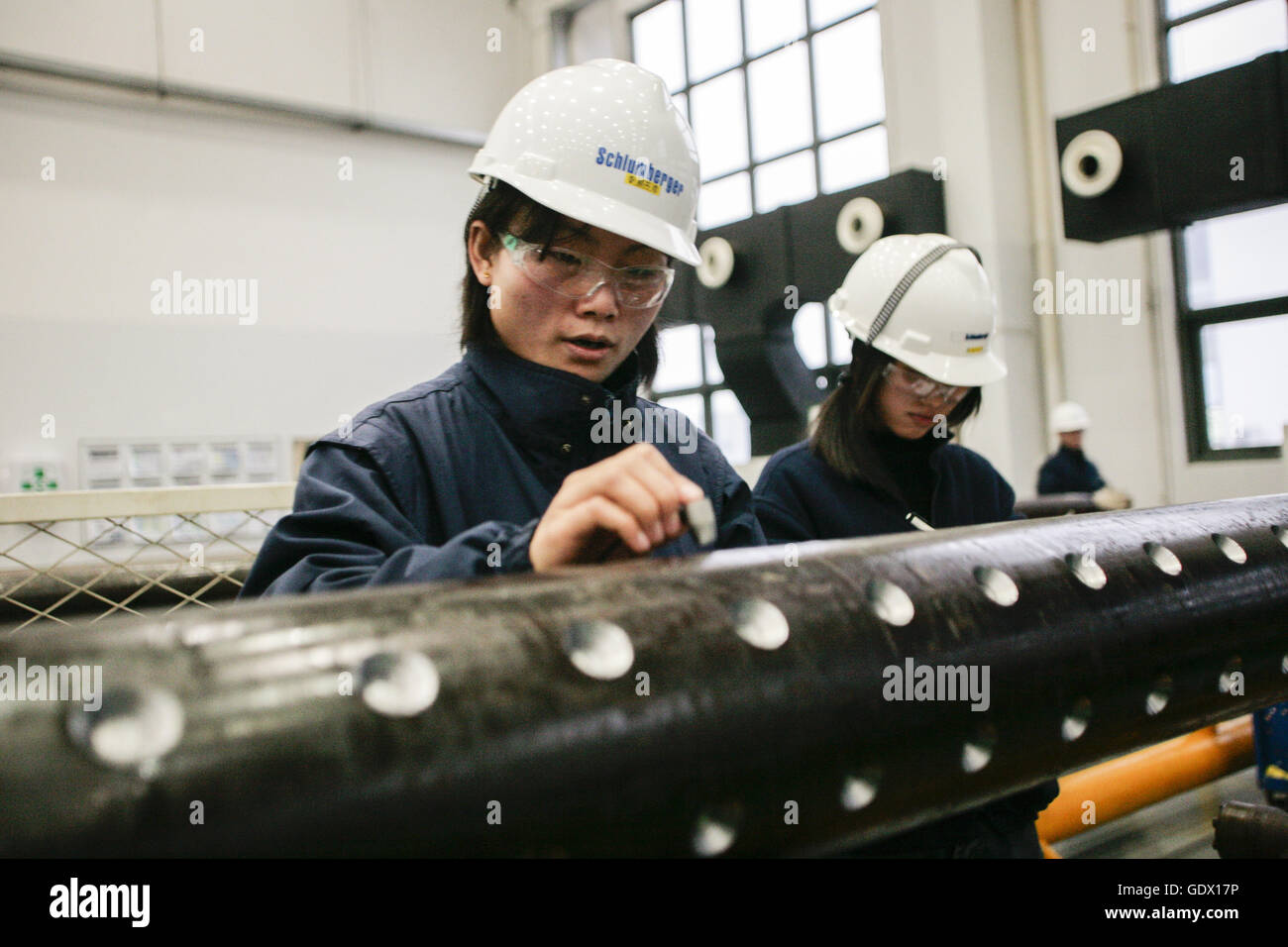 Workers work at a drilling pipe production line in a Schlumberger plant ...