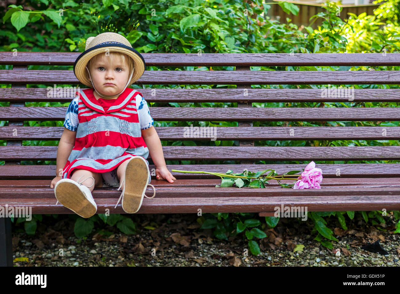 Cute sitting on a bench toddler looking grumpy Stock Photo - Alamy