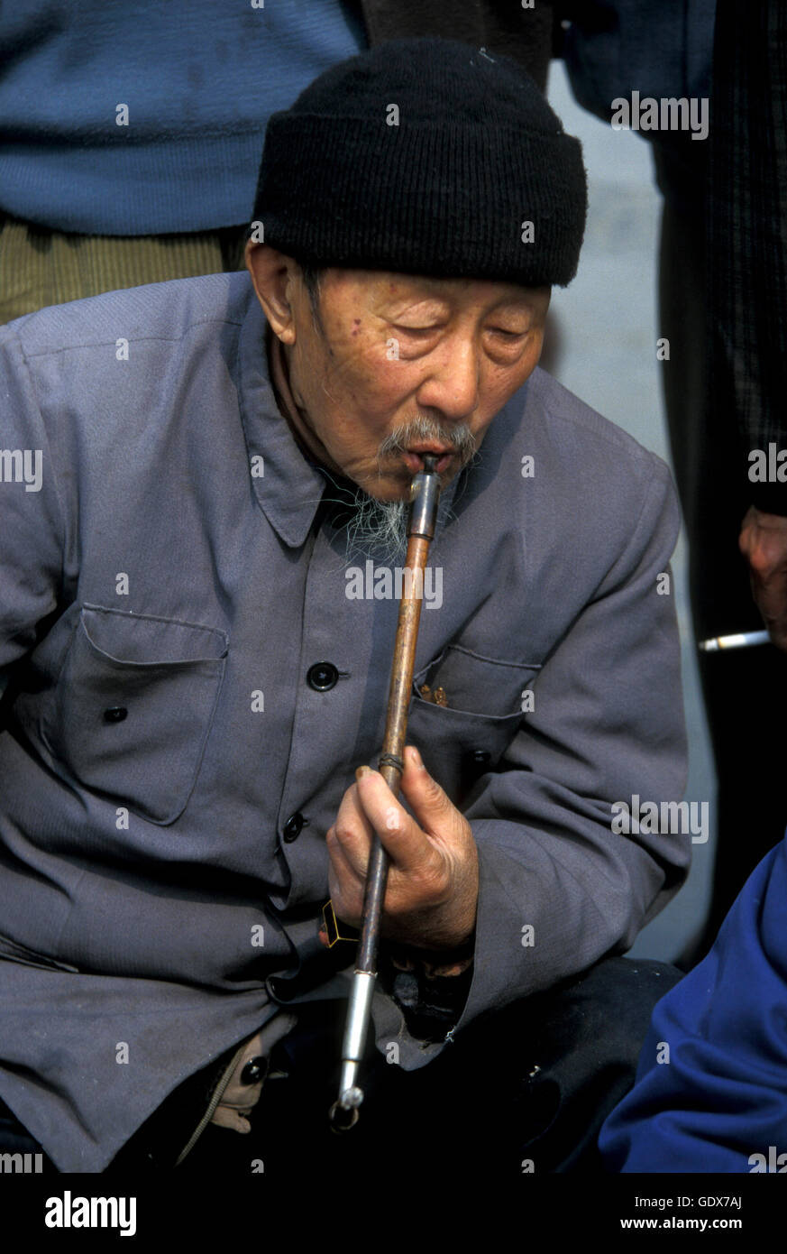 a chinese men smoking a traditional pipe in a parc in the city of ...