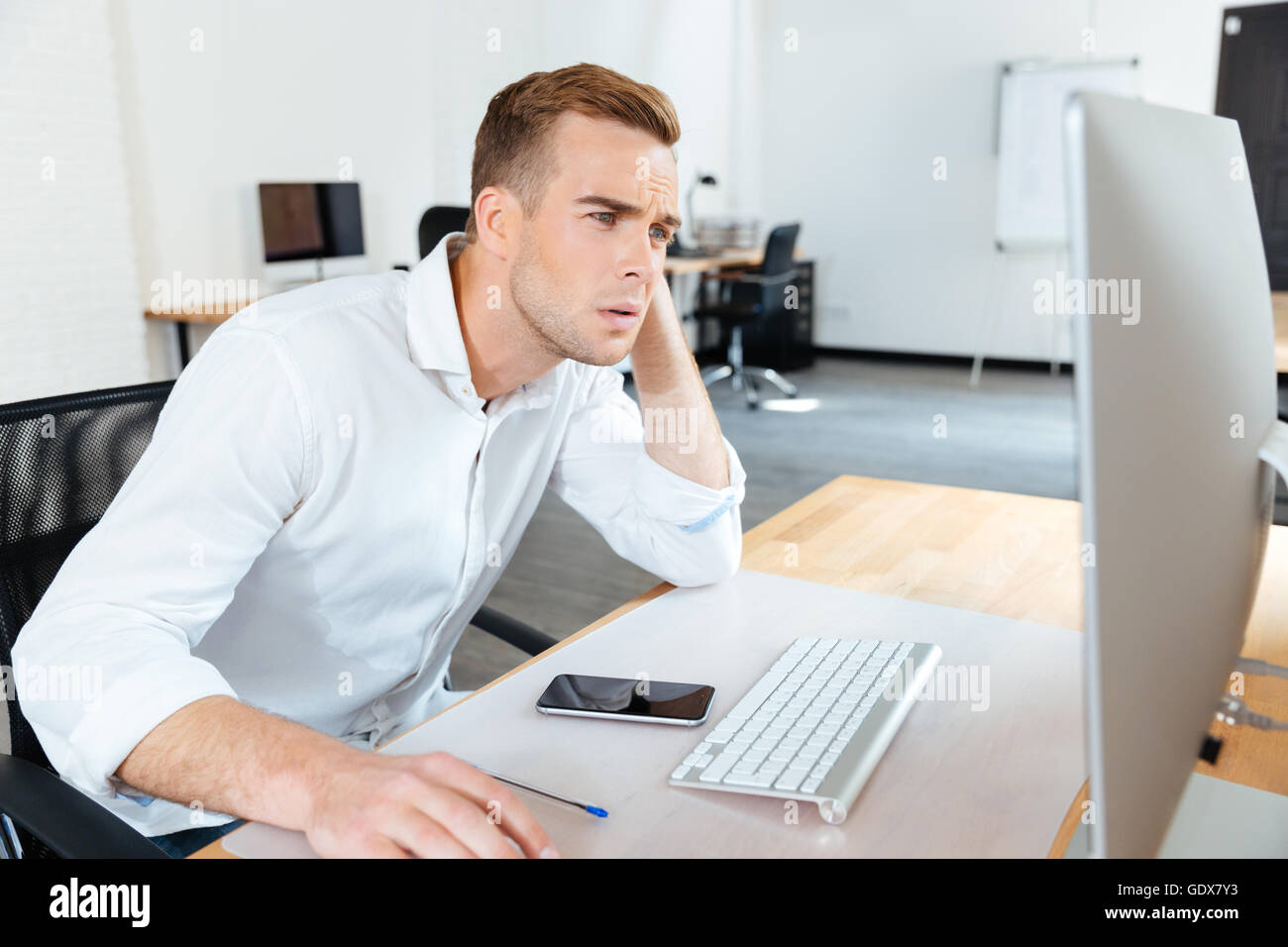 Thoughtful young businessman thinking and using computer in office ...
