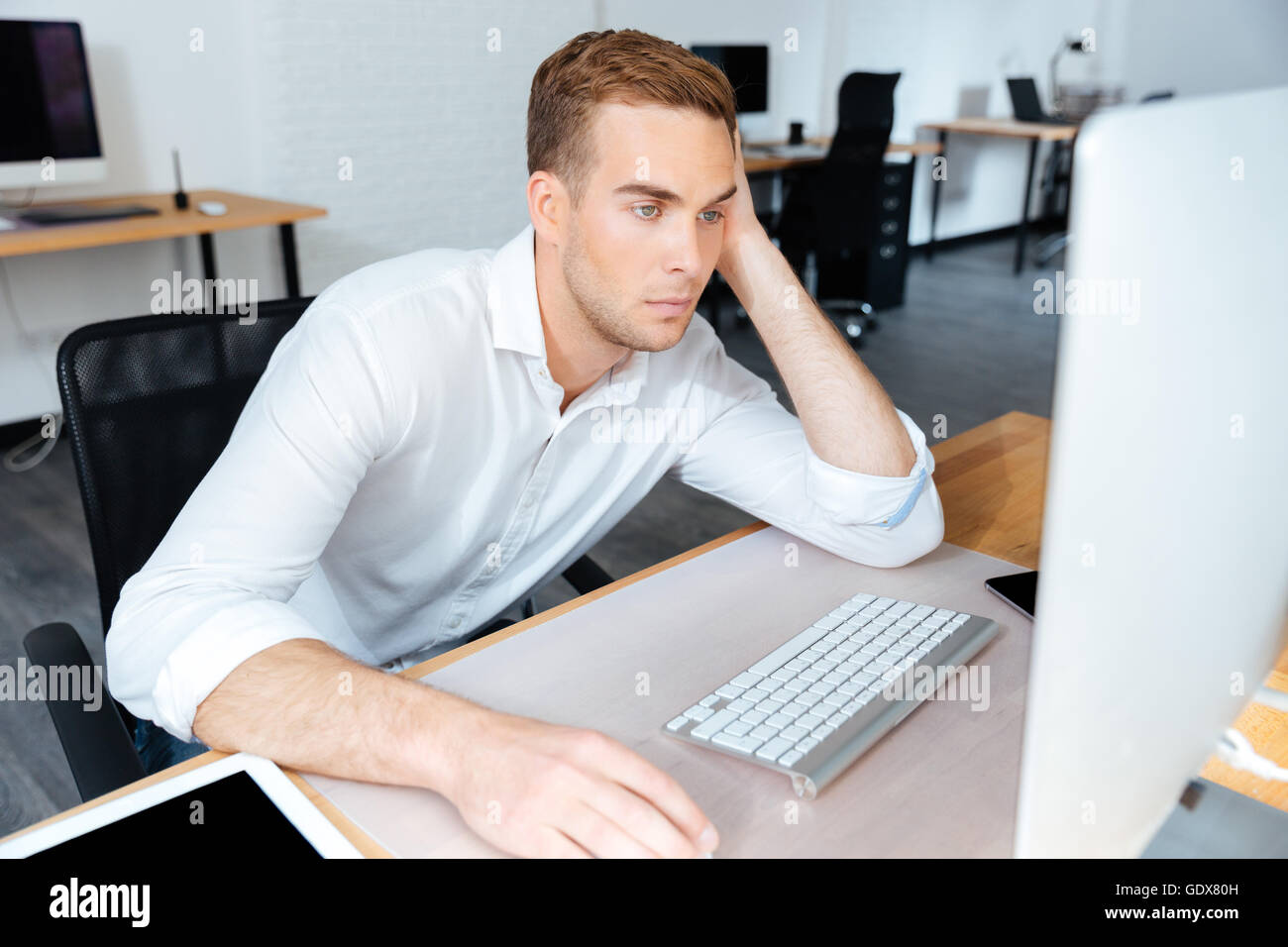 Tired bored young businessman sitting and working with computer in ...
