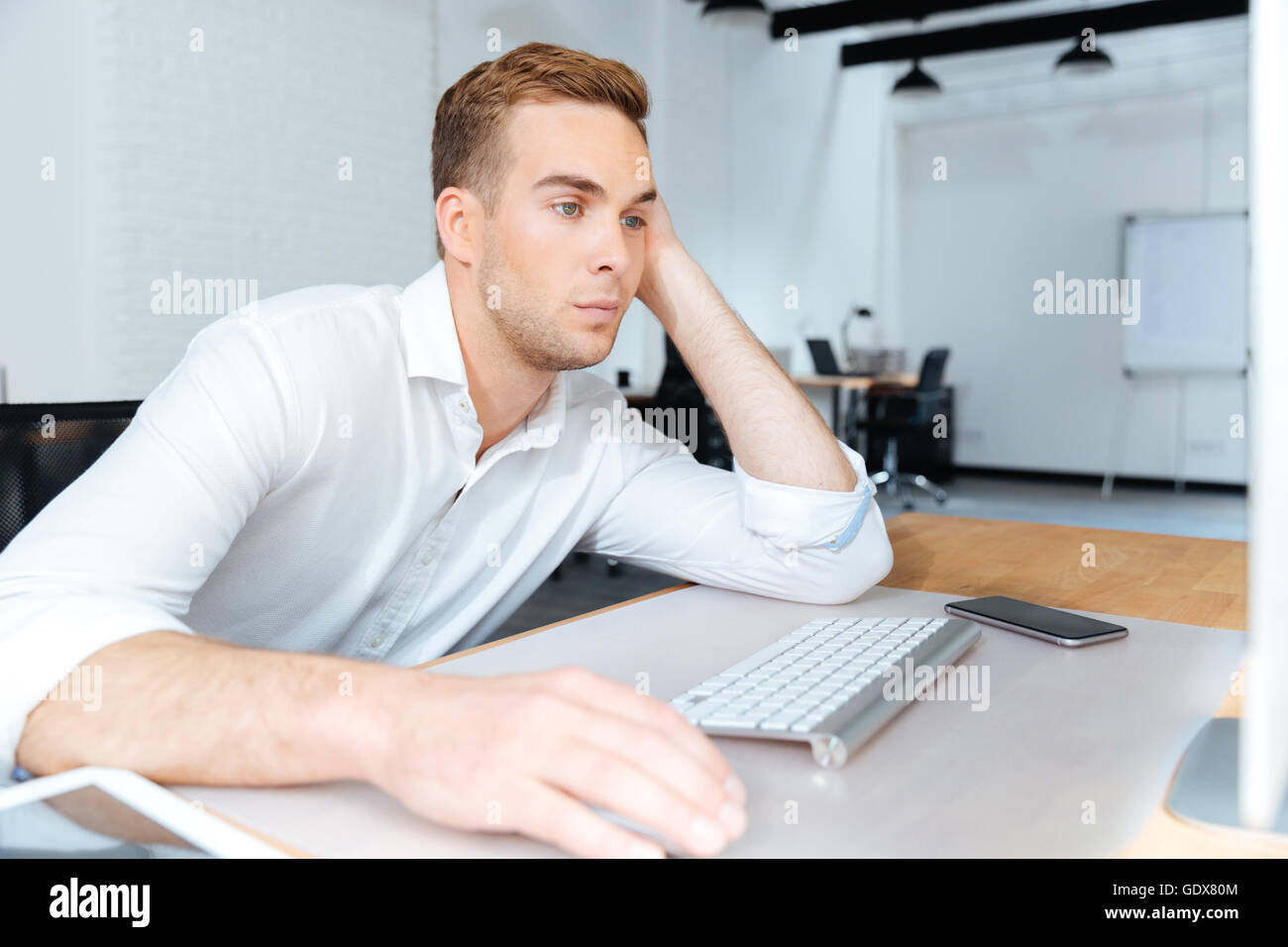 Sad bored young businessman sitting and working with computer in office ...
