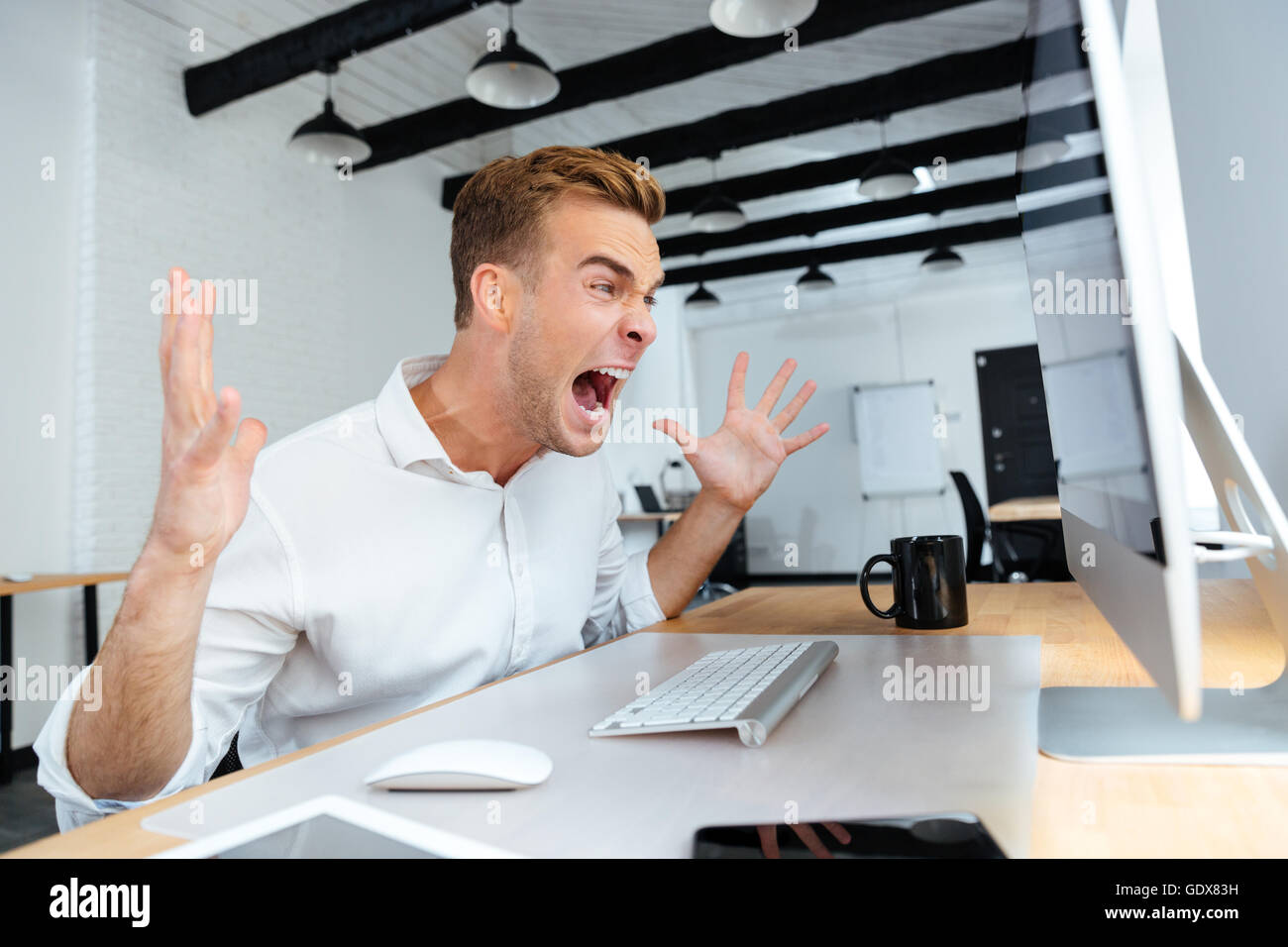 Furious angry young businessman working with computer and shouting ...