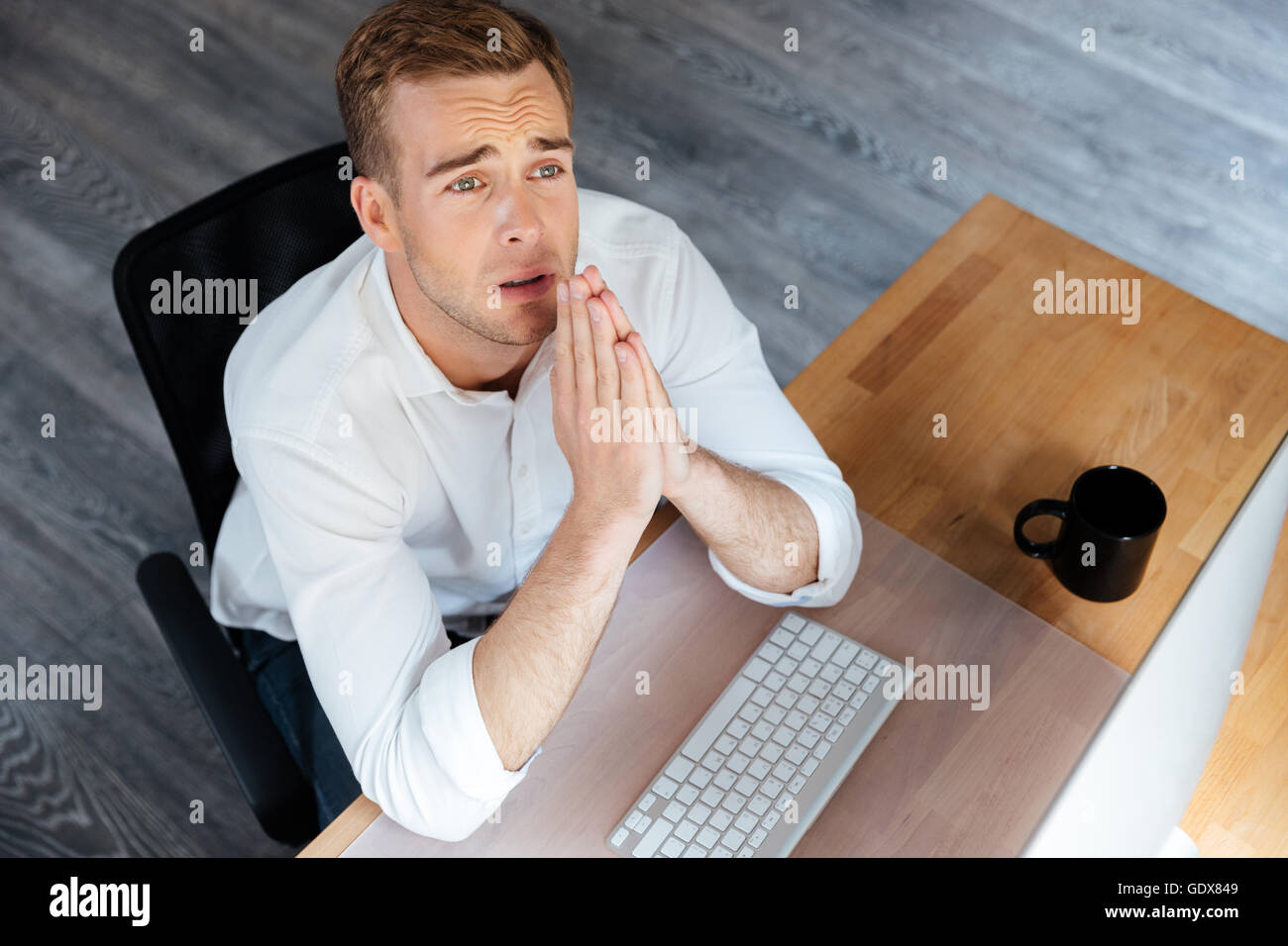 Top view of sad upset young businessman sitting and praying in office ...