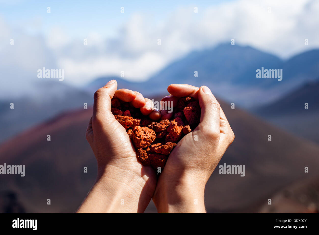 Hands forming a heart full of red volcanic rocks at Haleakala National ...