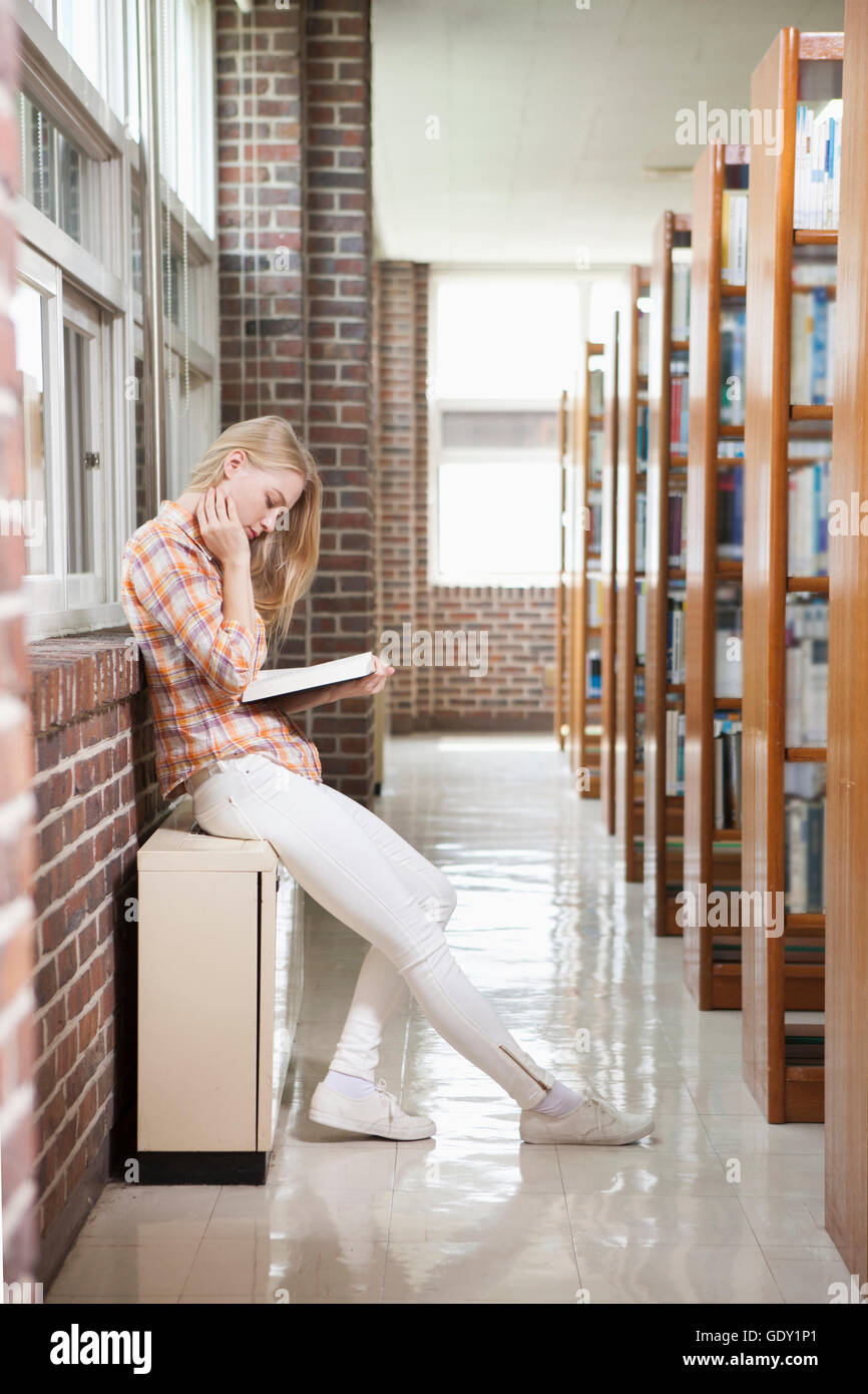 Side view of female college student reading a book at library looking ...