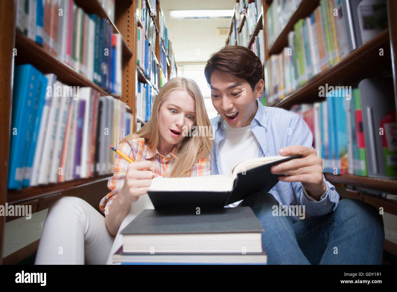 Two college students sharing a book at library looking down Stock Photo ...