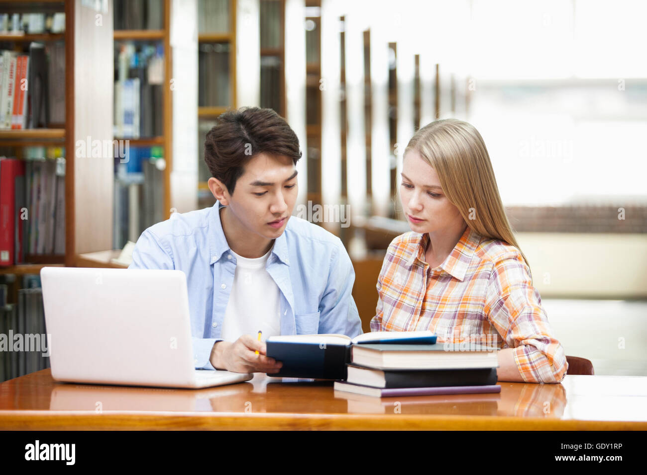 Portrait of young oriental man and young western woman sharing a book ...