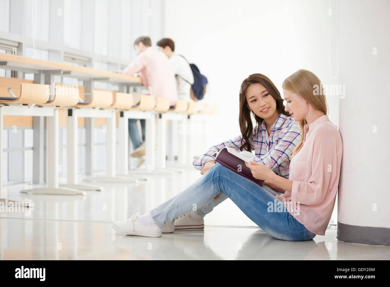 Side view of two female college students sitting and talking at library ...