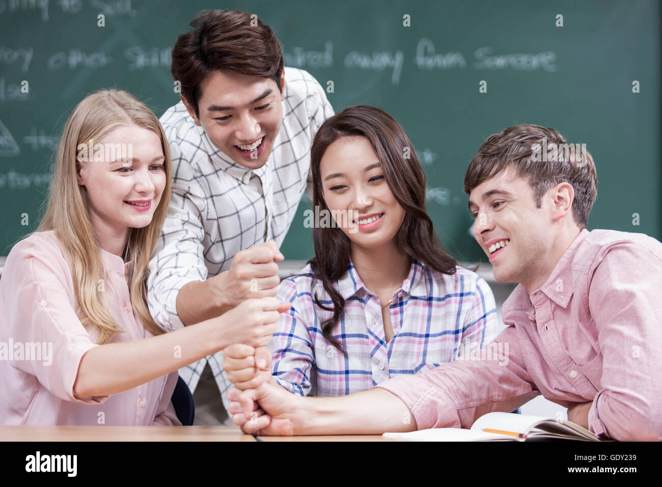 Portrait of four smiling college students putting their hands together ...