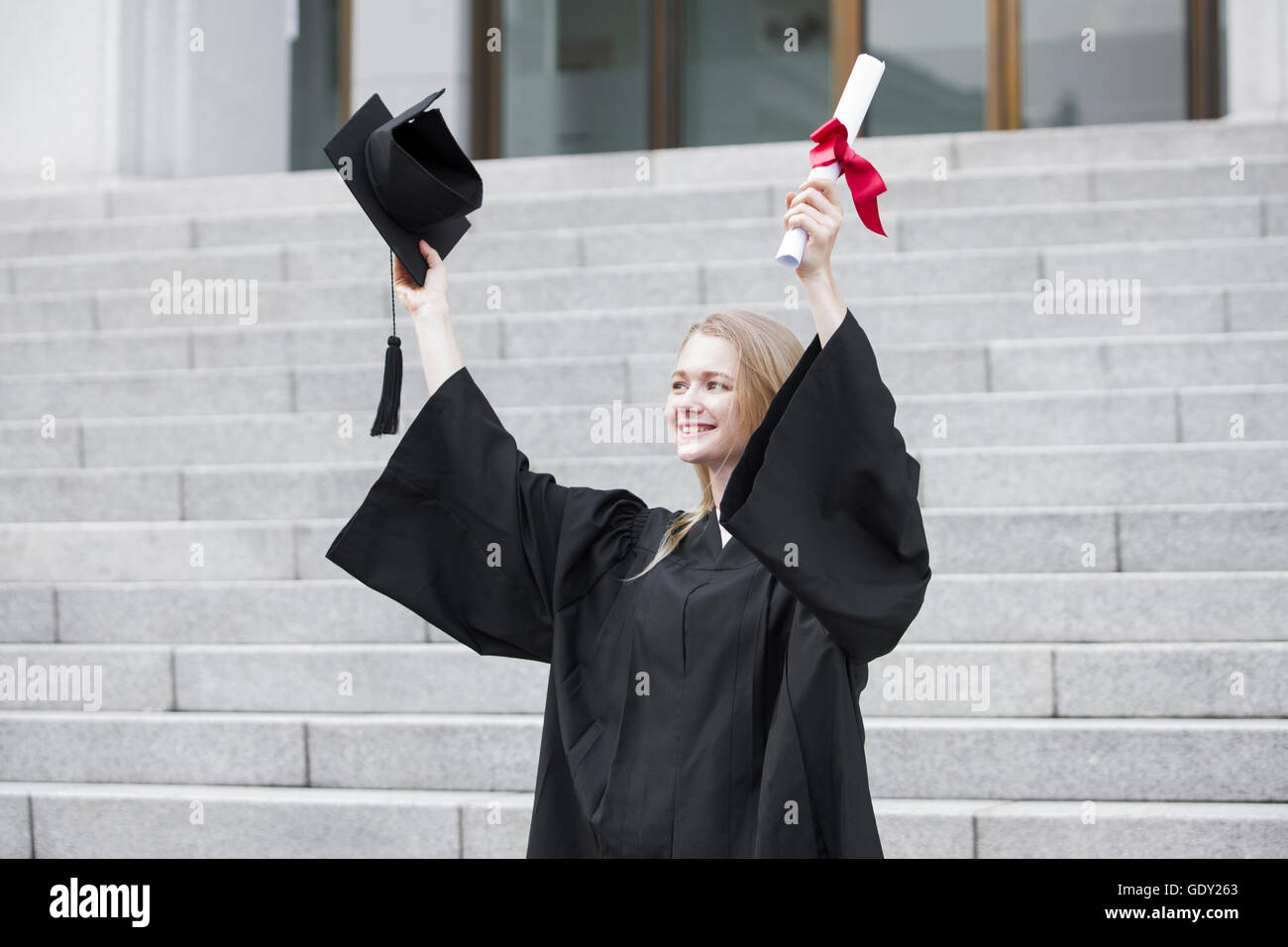 Side view p portraitof smiling college graduate in gown holding her hat ...