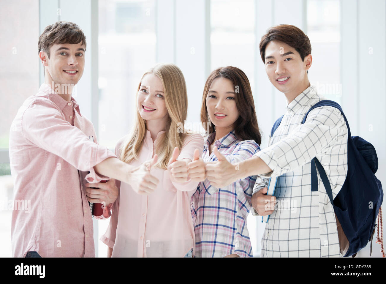 Portrait of four smiling global college students showing thumb-up signs ...
