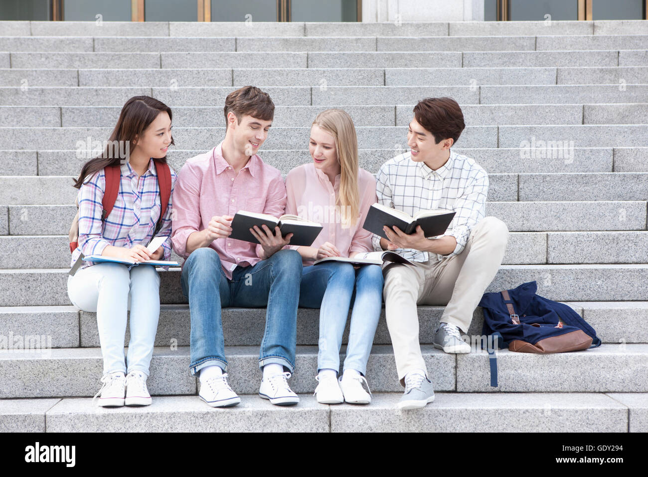 Four smiling college students with books sitting on stairs Stock Photo ...