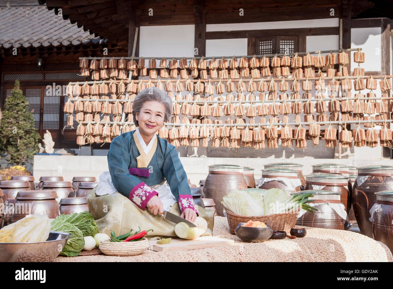 Smiling old woman in traditional Korean clothes cutting vegetables for ...