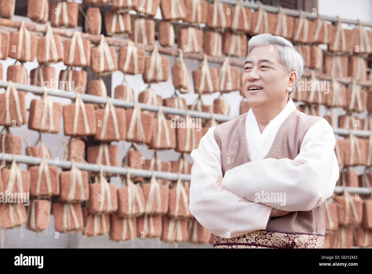 Smiling old man in traditional Korean clothes folding his arms against ...