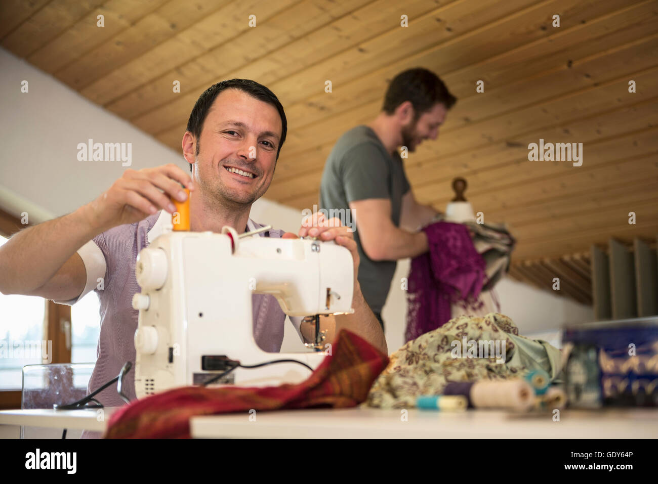Male dressmaker stitching cloth on sewing machine with his colleague in ...