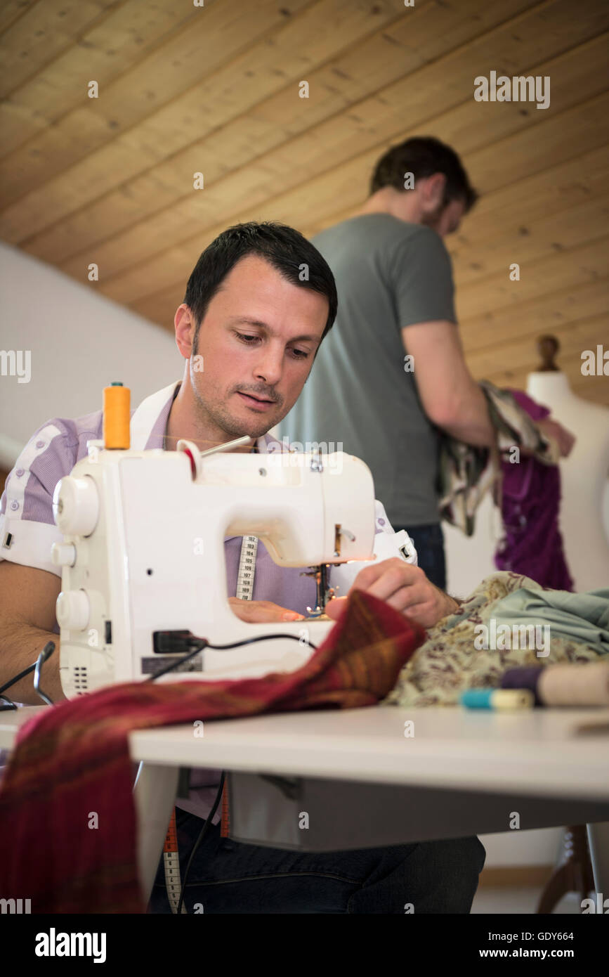 Male dressmaker stitching cloth on sewing machine with his colleague in ...