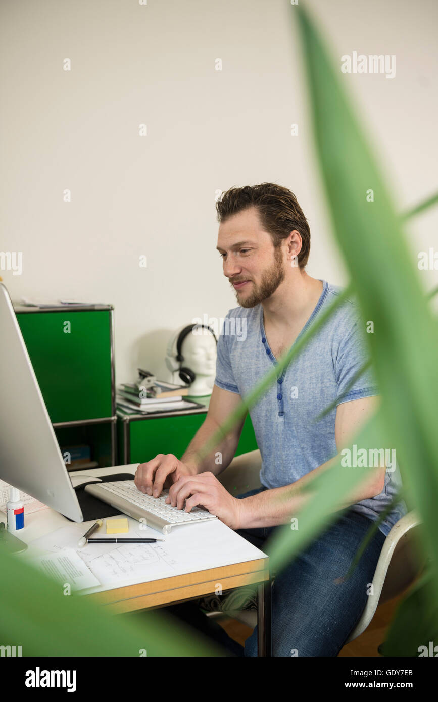 Mid adult man working on computer in living room and smiling, Munich ...