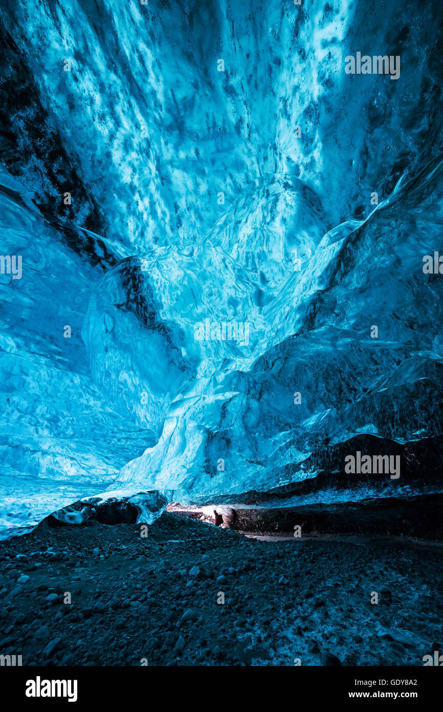 Man inside an immense ice cave, very small in comparison to the size of ...